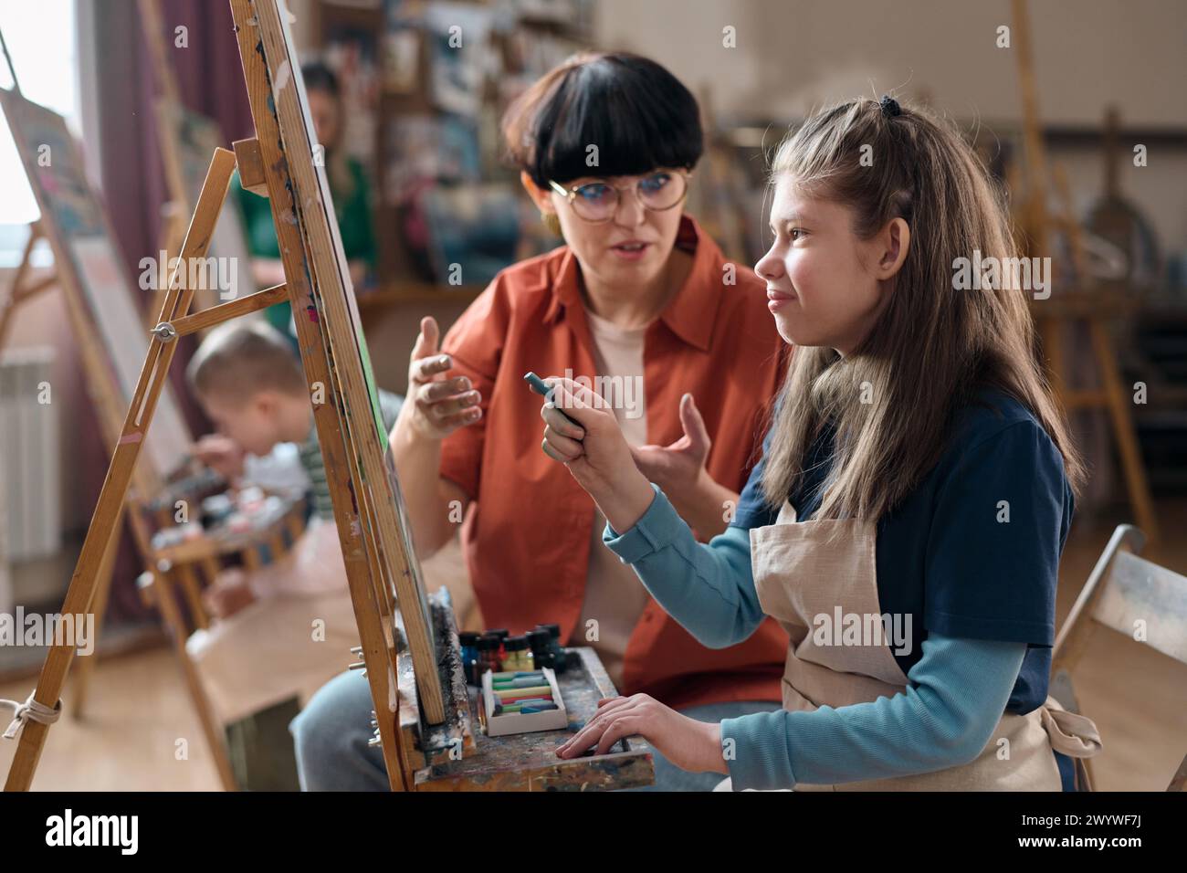 Side view portrait of smiling girl with disability painting on easel ...