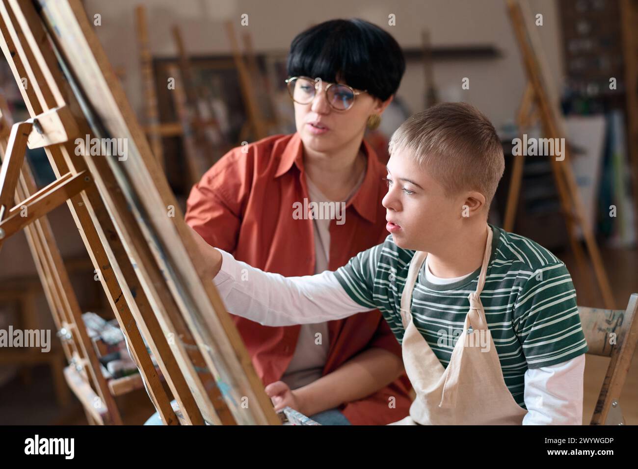 Side view portrait of young boy with Down syndrome painting on easel in ...