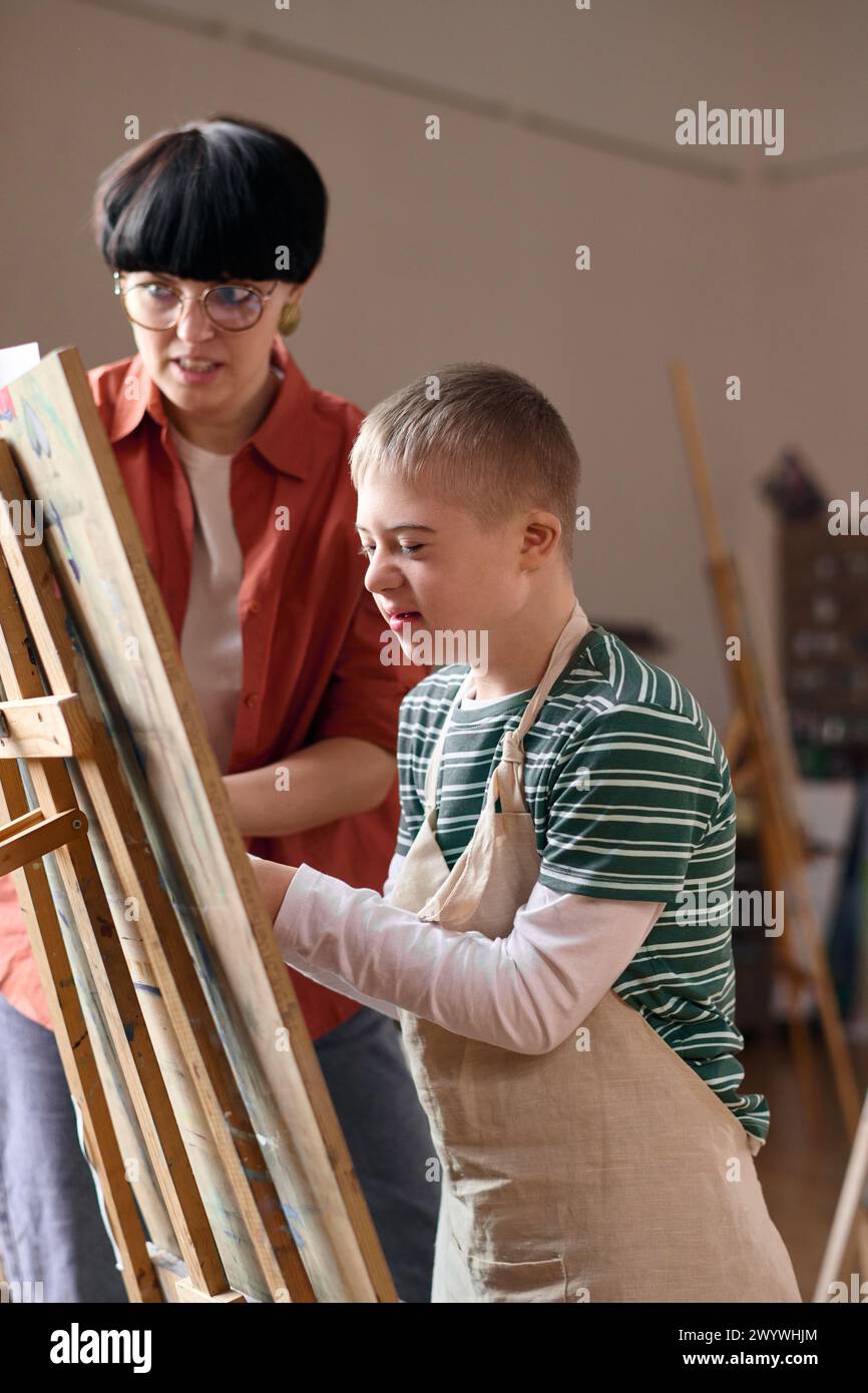 Vertical portrait of smiling boy with disability painting on canvas in ...