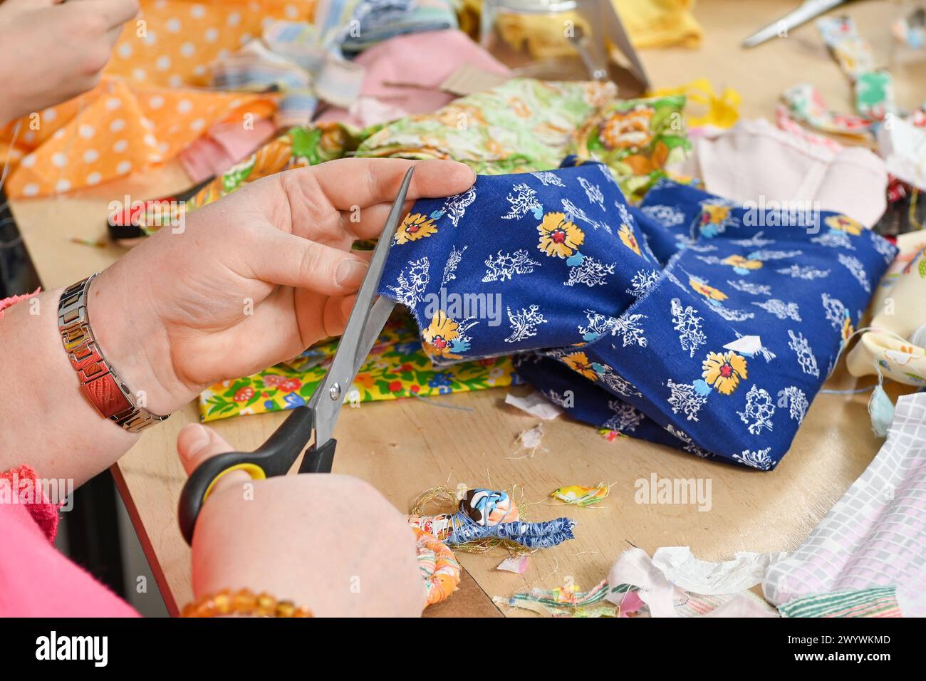 In a cozy sewing studio, a womans hands carefully cut a vibrant blue ...