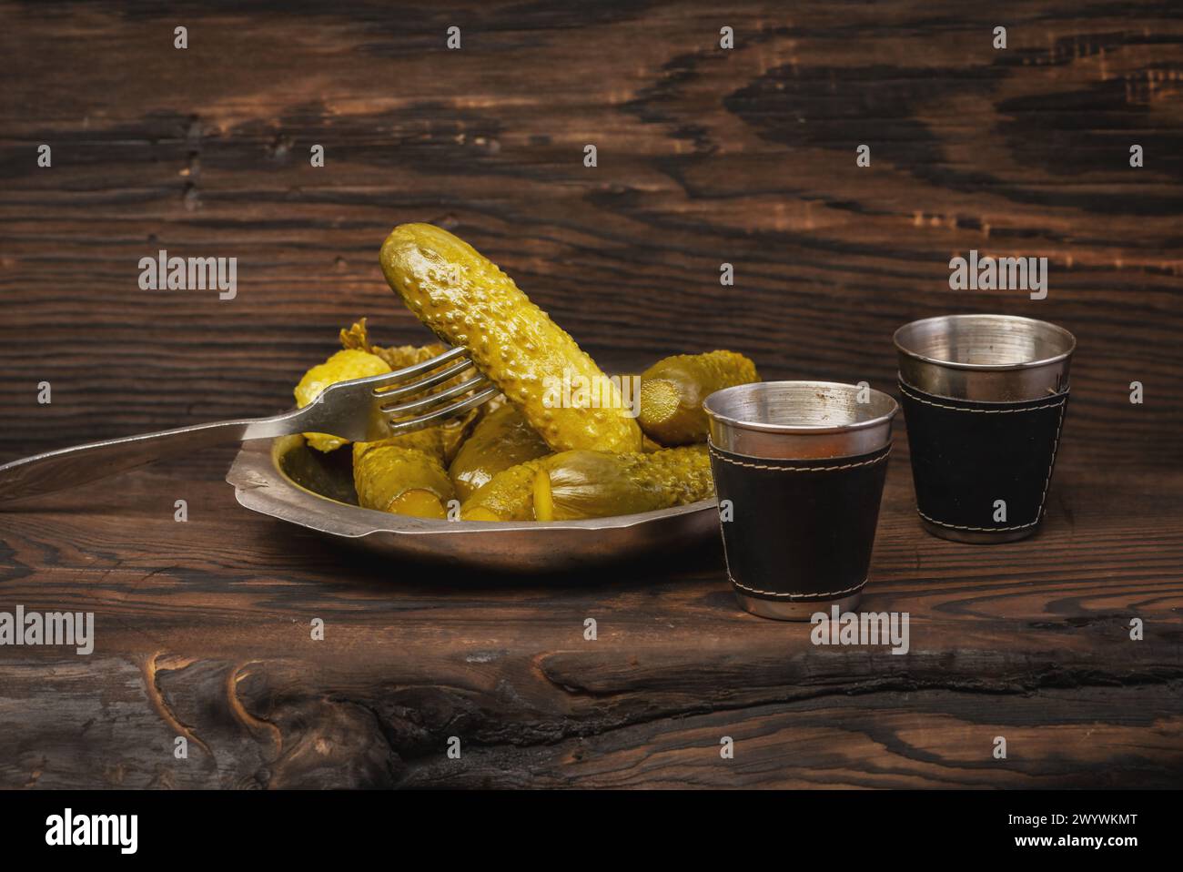Rustic wooden table with assorted pickles on a metal plate and cups of ...