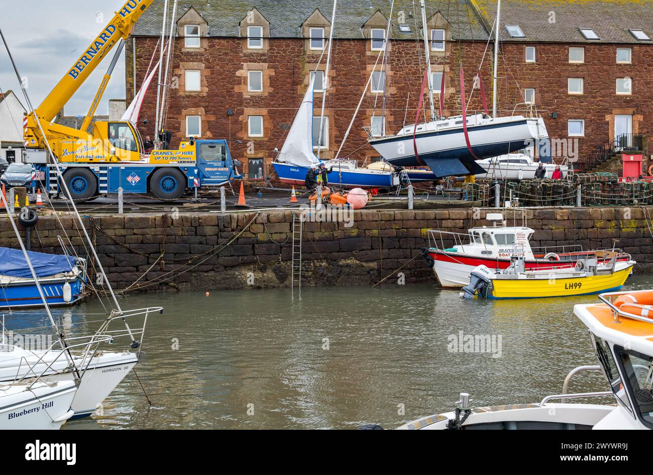 Crane lifting sailing boat into water, North Berwick harbour, East ...