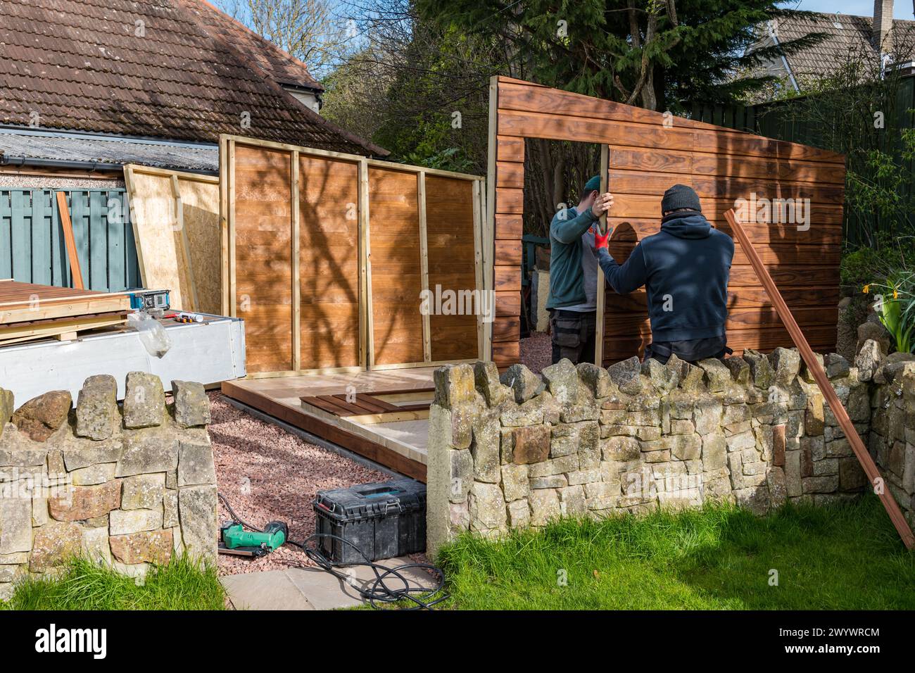 Joiners and workmen constructing the walls of a shed and garden room ...