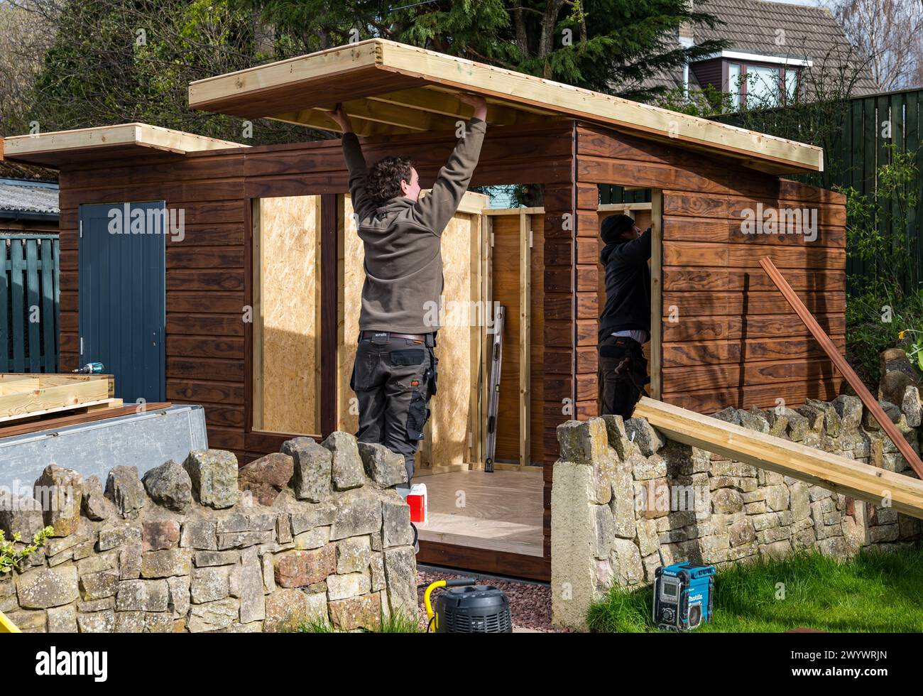 Joiners and workmen fitting a roof to construct a shed and garden room ...