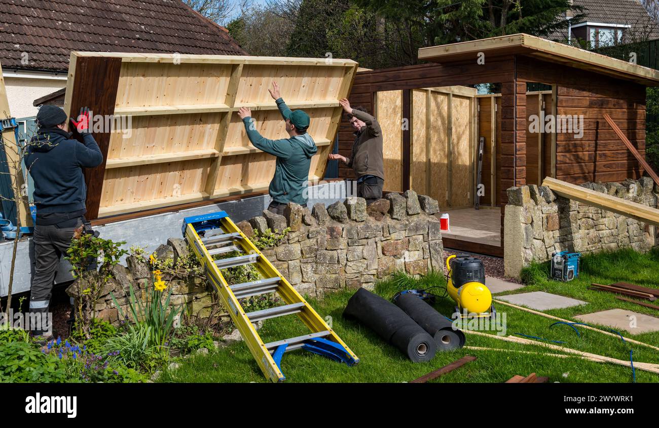 Joiners and workmen fitting a roof to construct a shed and garden room ...