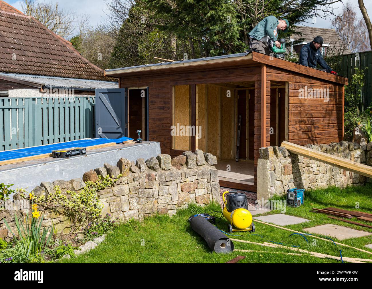 Joiners and workmen fitting a roof to construct a shed and garden room ...