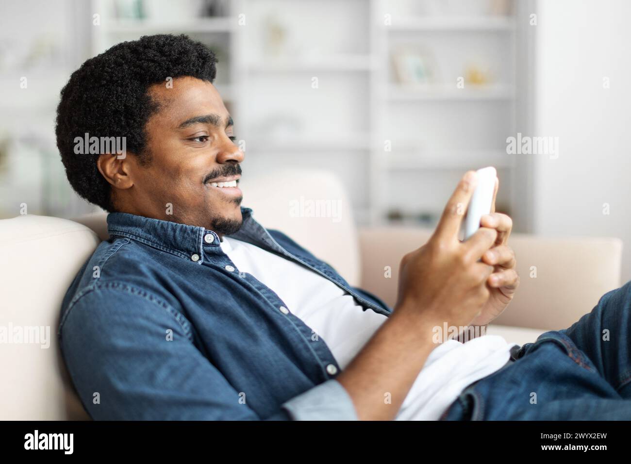Smiling Black Man Engaged With Smartphone on Couch During Daytime Stock ...