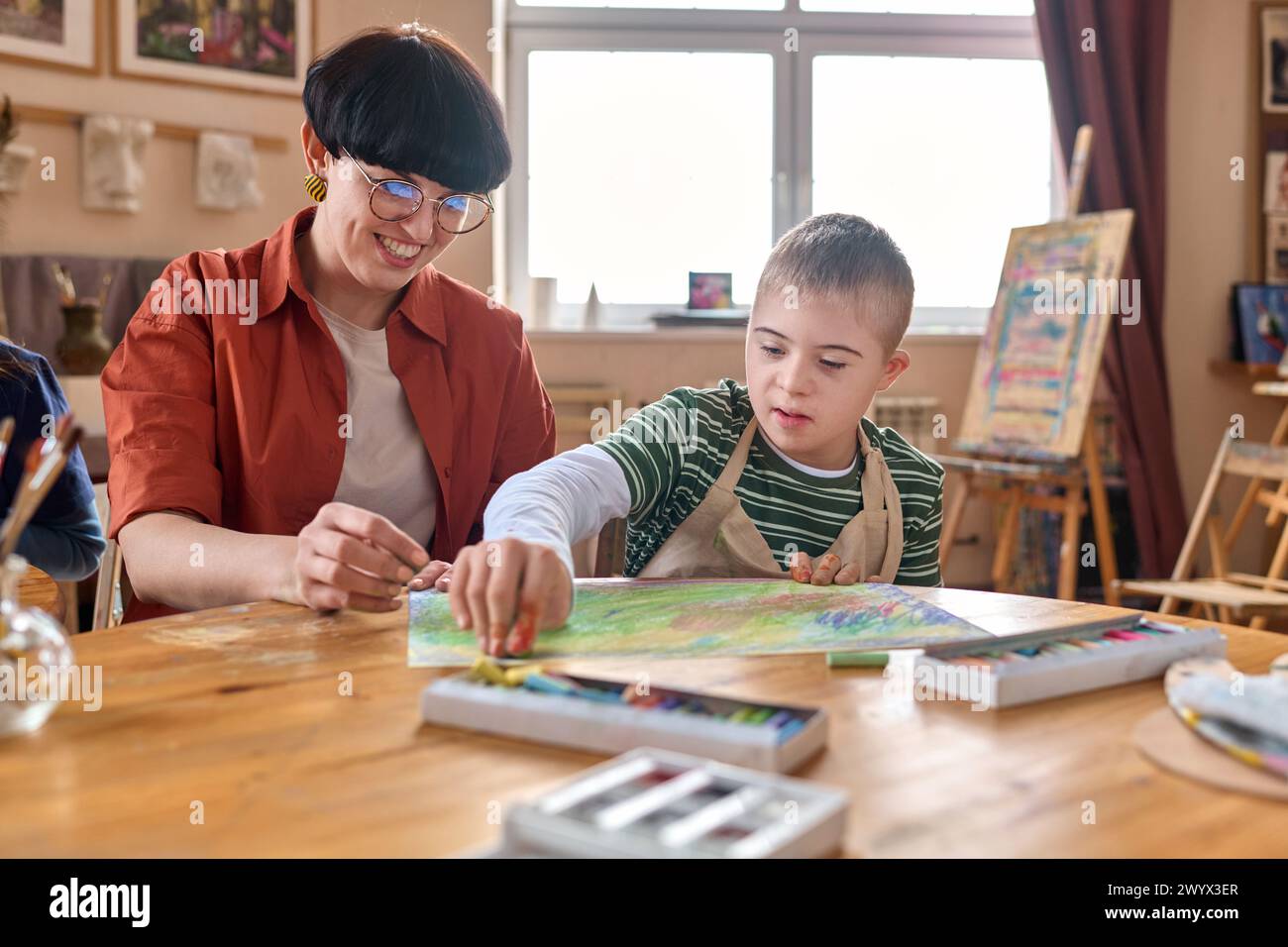 Portrait of young boy with Down syndrome enjoying art class with female ...