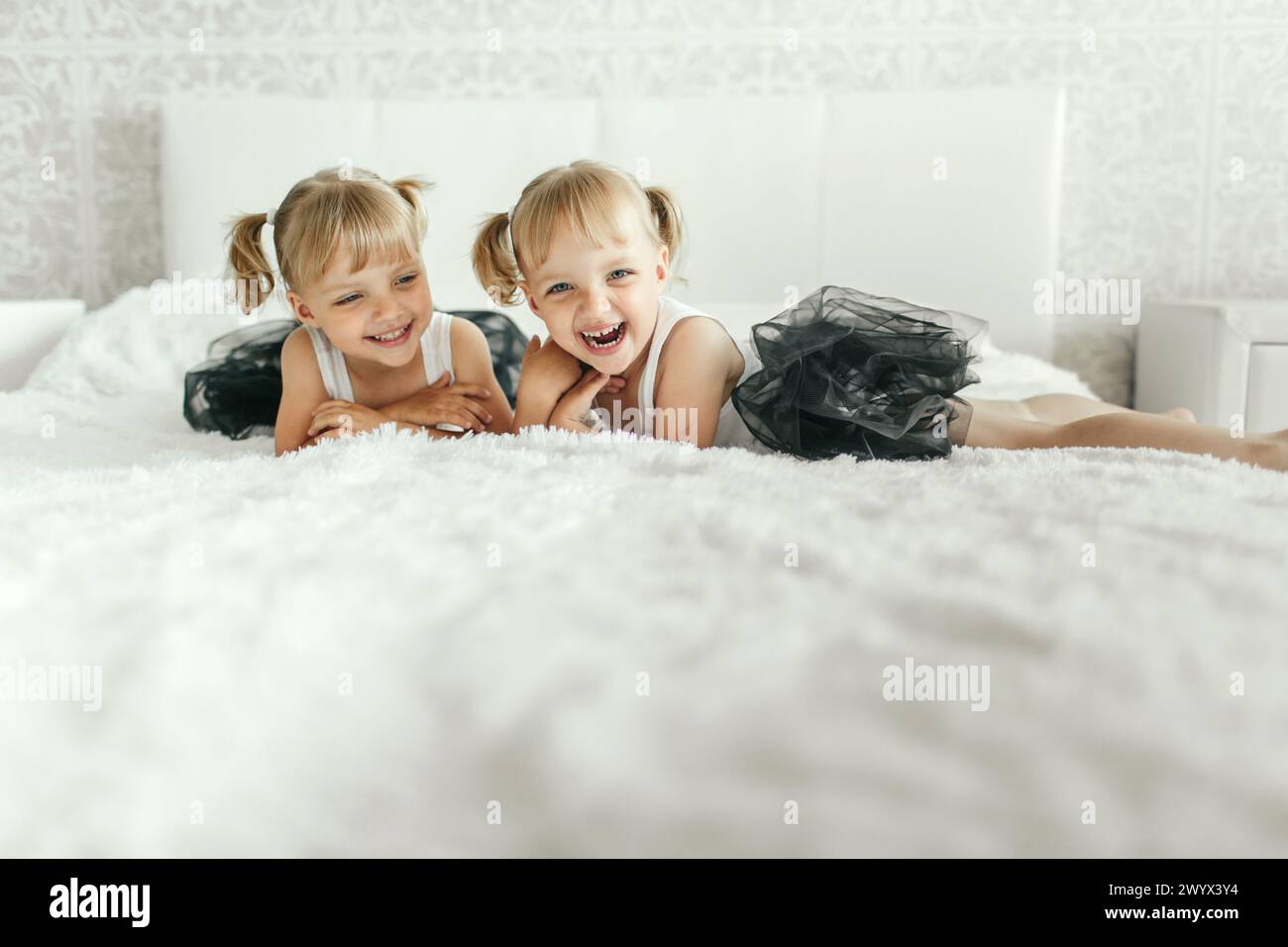 Two young girls are laying on a bed, laughing joyfully together Stock ...