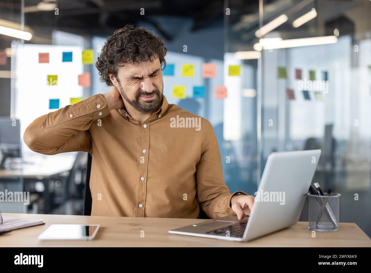 A male office employee feels sharp neck pain while working on his ...