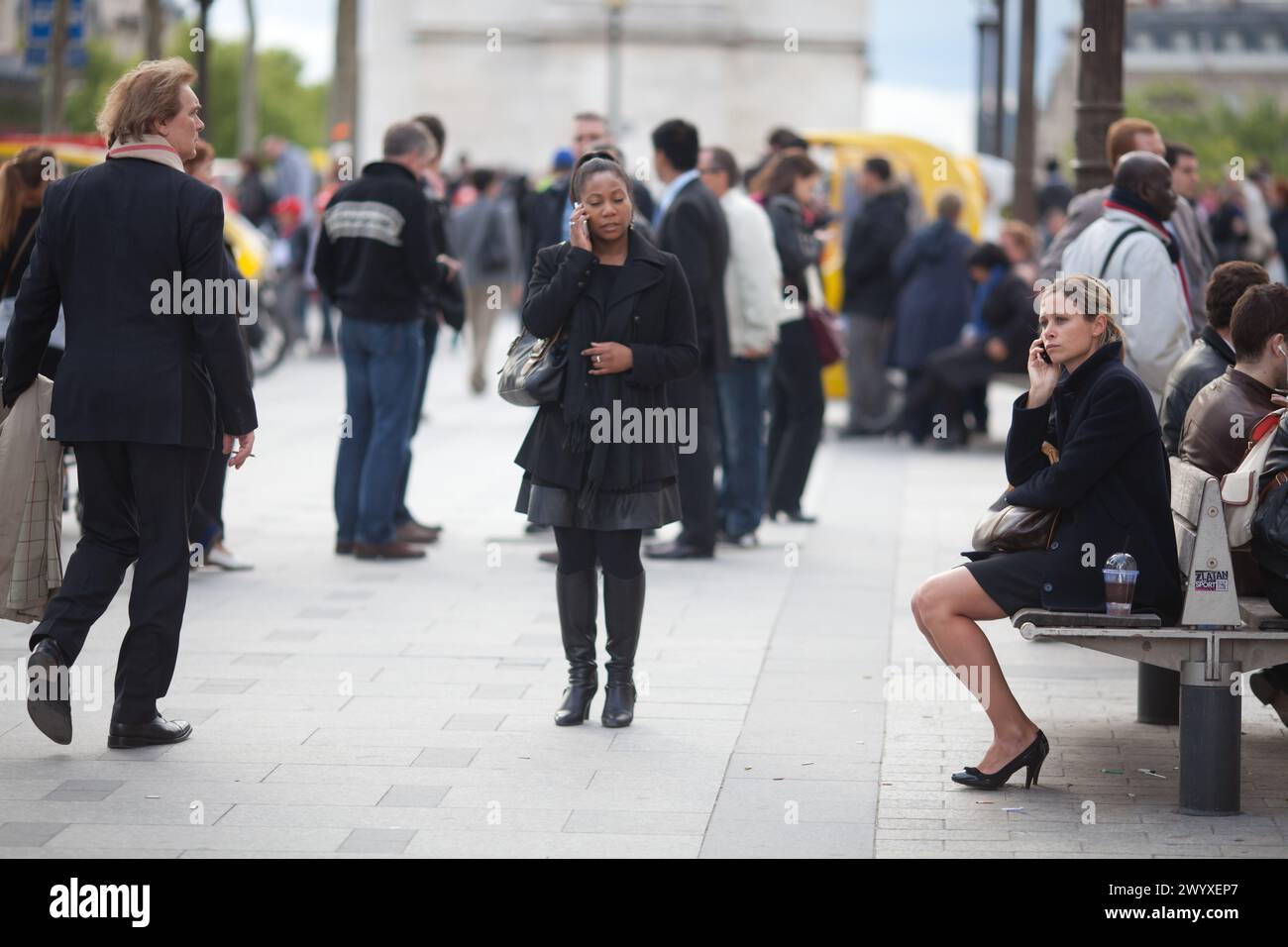 Girl sitting on a bench and calling while another is standing in front ...
