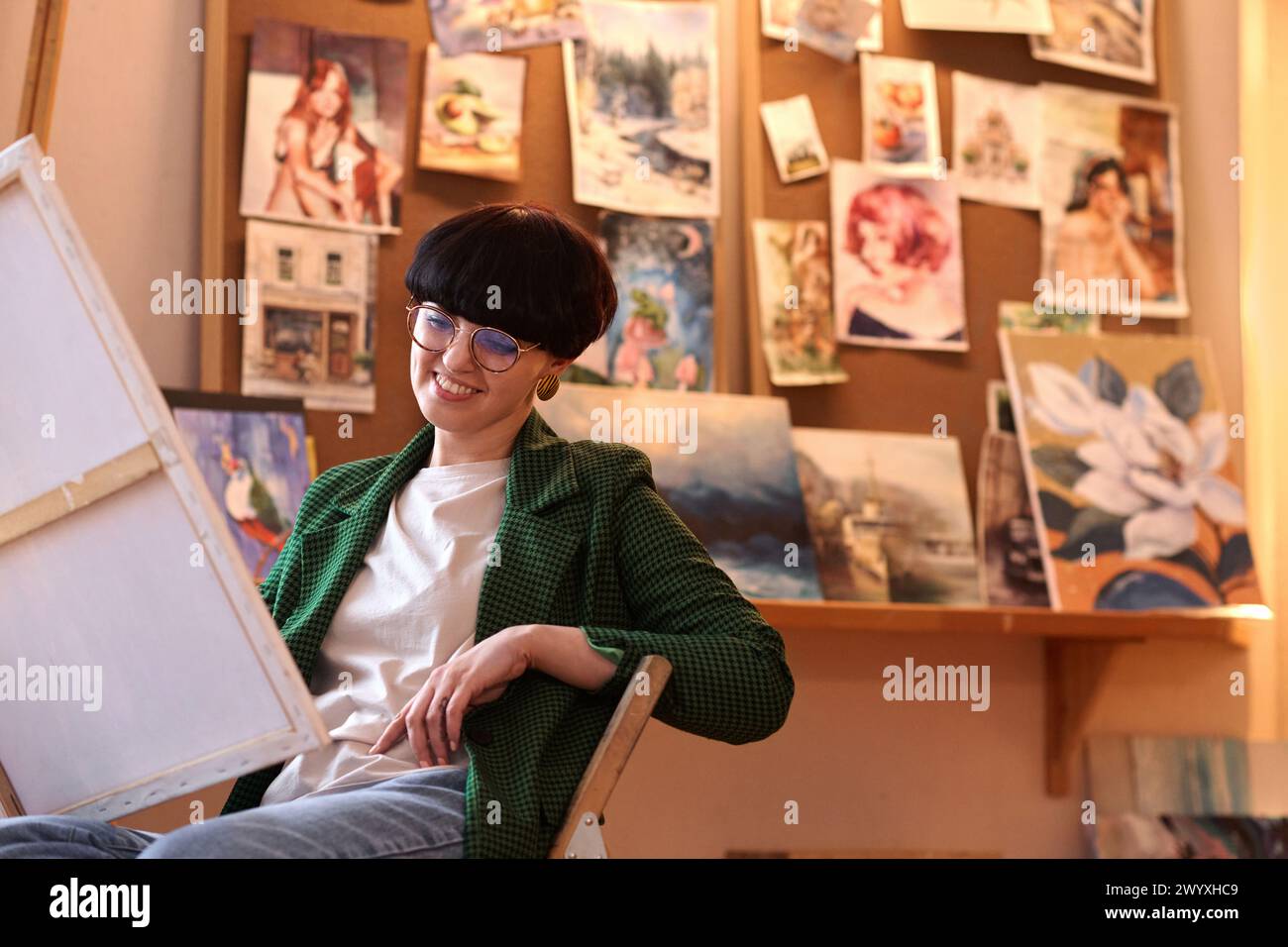 Portrait of smiling woman artist looking at picture in art studio or ...