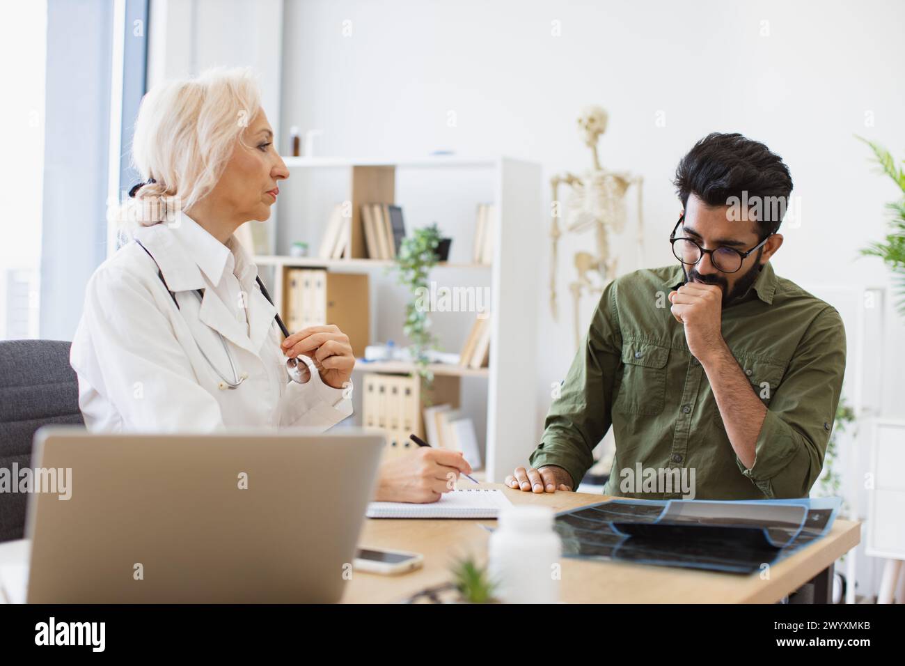 Female general practitioner communicating with young coughing patient ...
