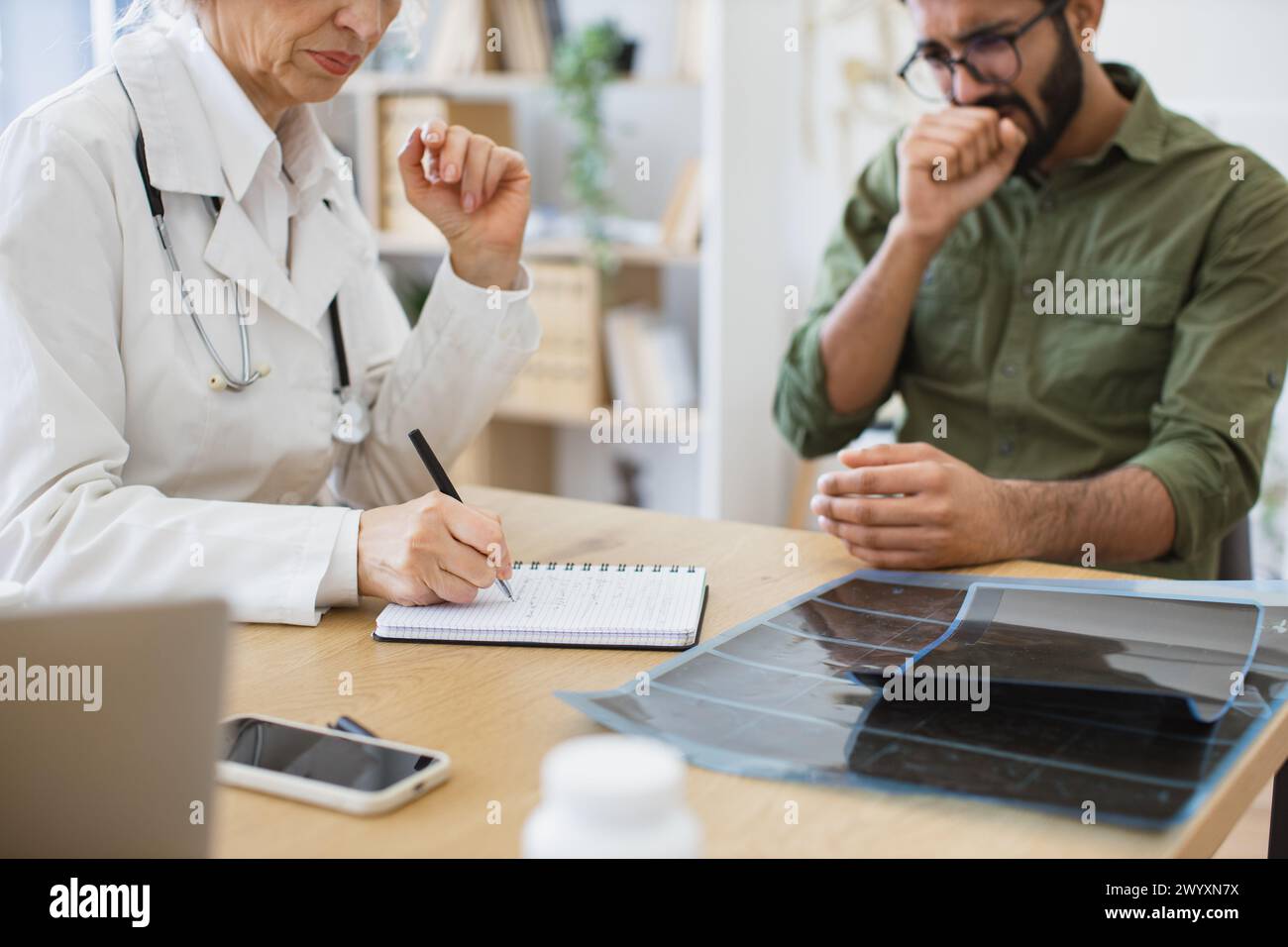 Female general practitioner communicating with young coughing patient ...