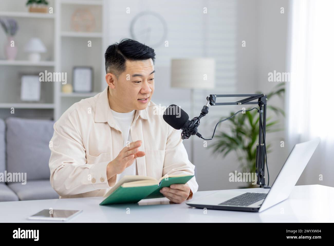Engaged Asian man recording a podcast at his home studio, with a book ...