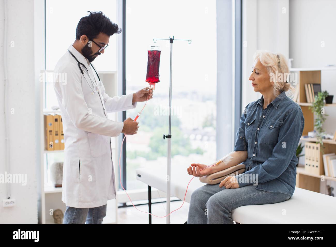 Elderly woman receiving blood transfusion looking at medical doctor ...