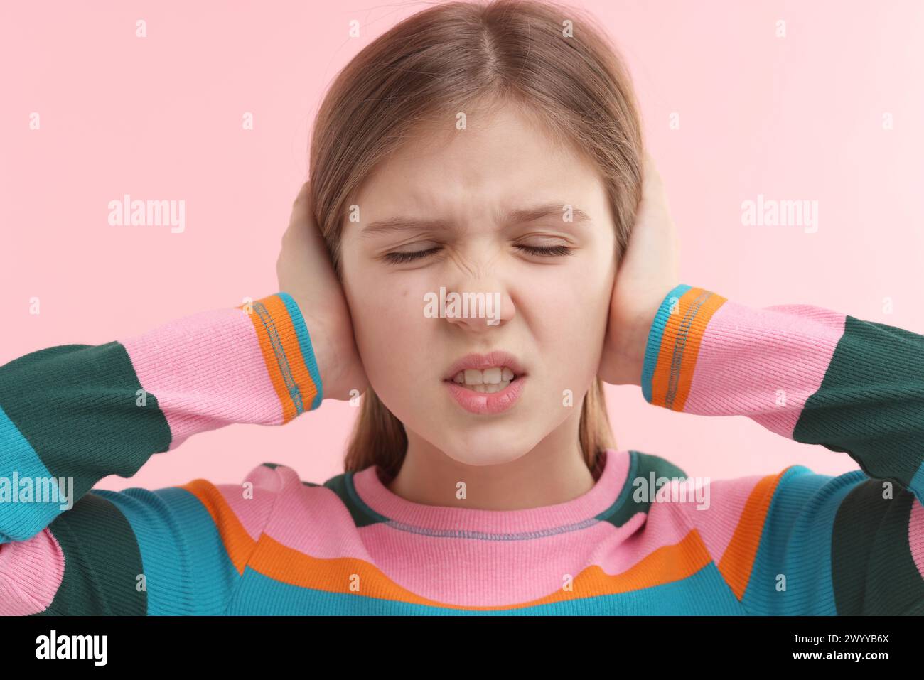 Hearing problem. Little girl suffering from ear pain on pink background ...