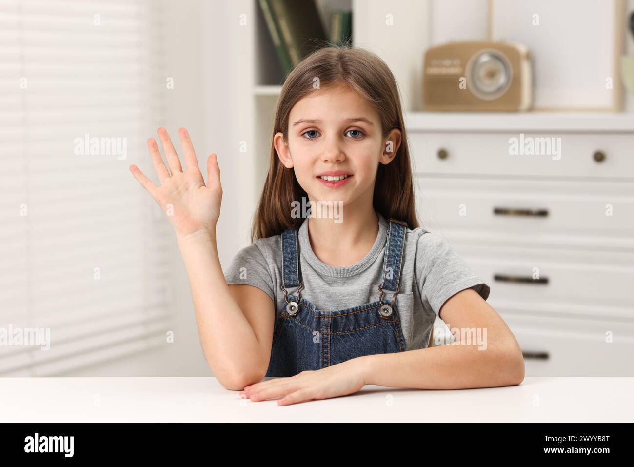 Happy little girl waving hello at white table indoors Stock Photo - Alamy