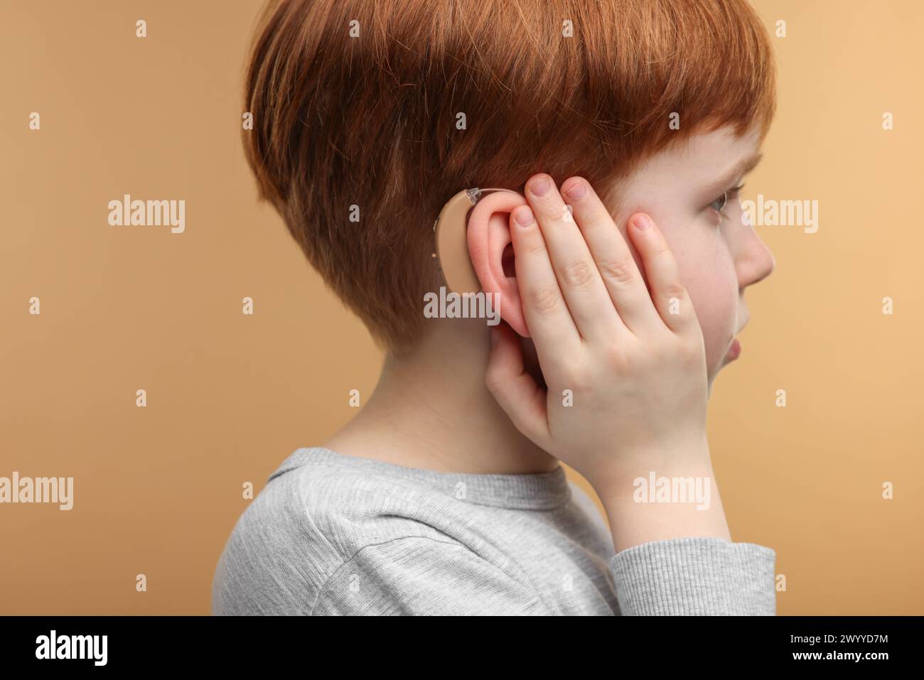 Little boy with hearing aid on pale brown background Stock Photo - Alamy