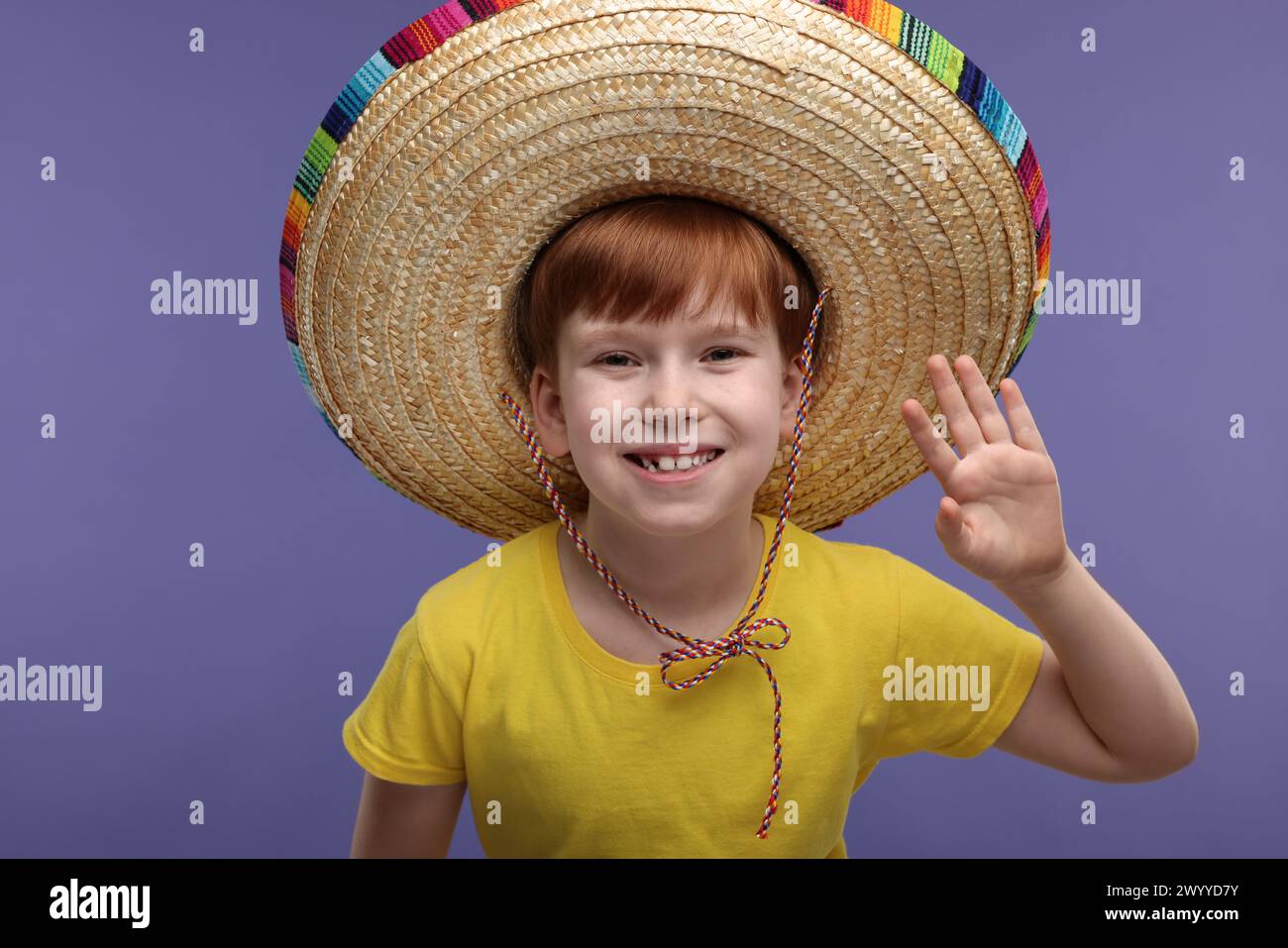 Cute boy in Mexican sombrero hat waving hello on violet background ...