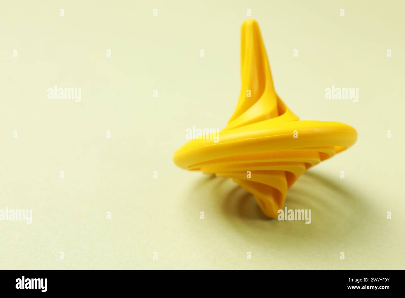 One yellow spinning top on green background, closeup. Space for text ...