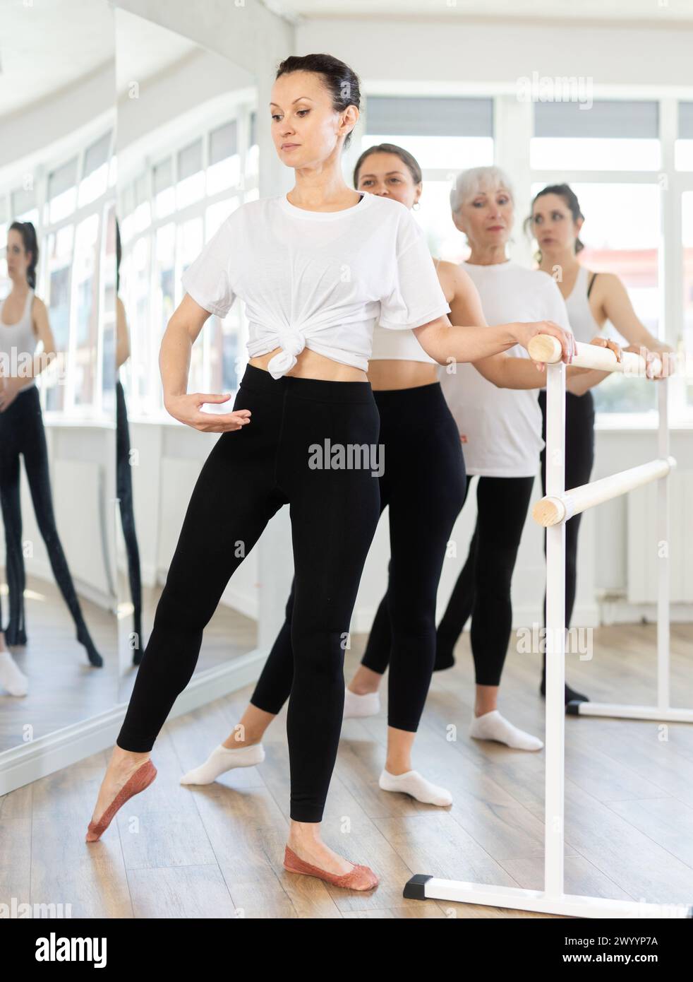 Graceful women of different ages practice at ballet stand in fifth ...