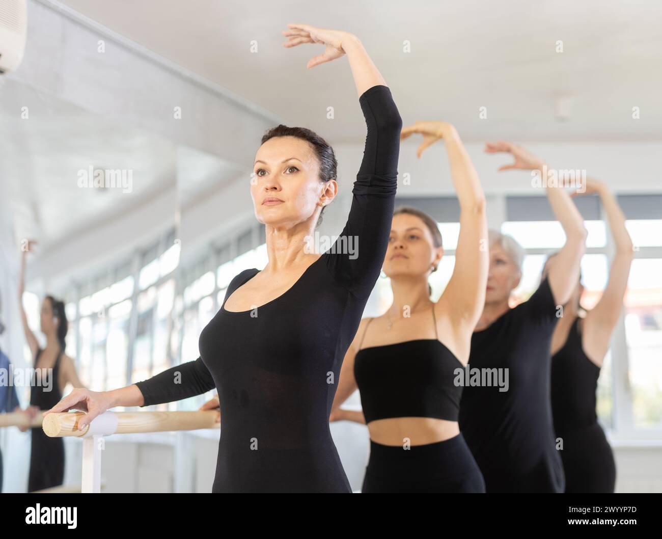 Woman maintaining third position at ballet barre at group rehearsal ...