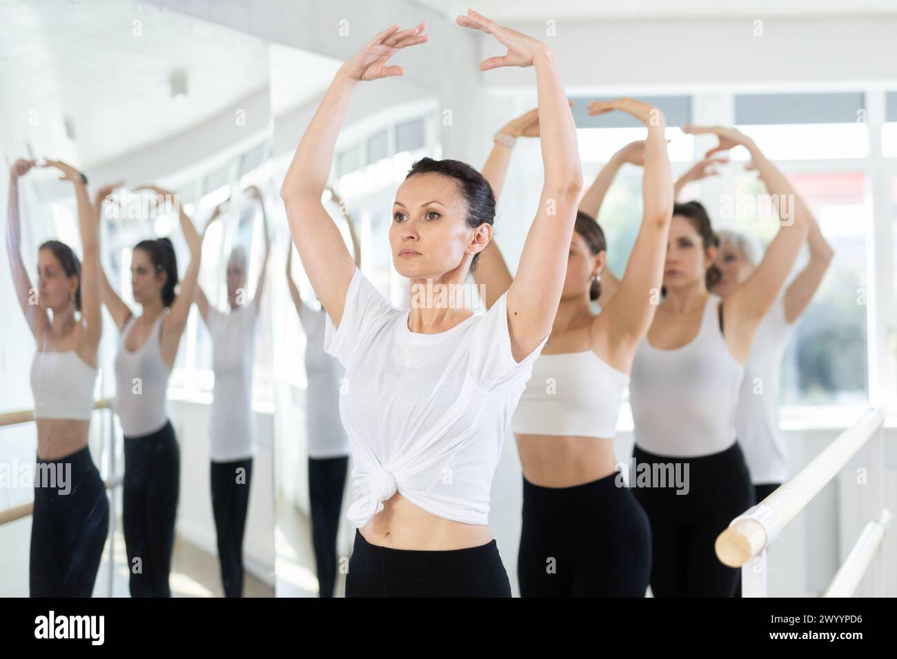 Female ballet dancers doing various ballet movements at ballet barre in ...