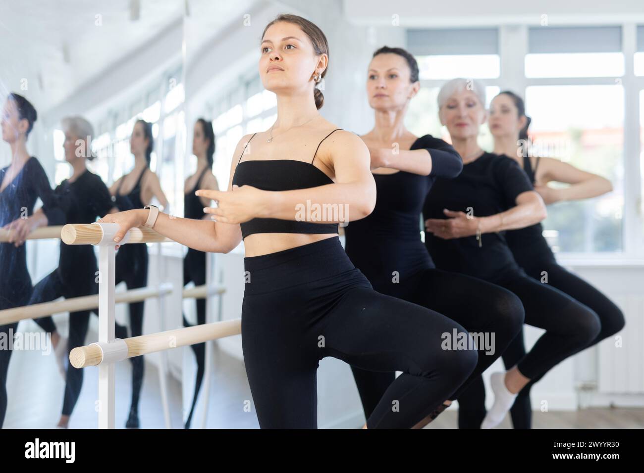 Young girl practicing in passe position at barre during group ballet ...