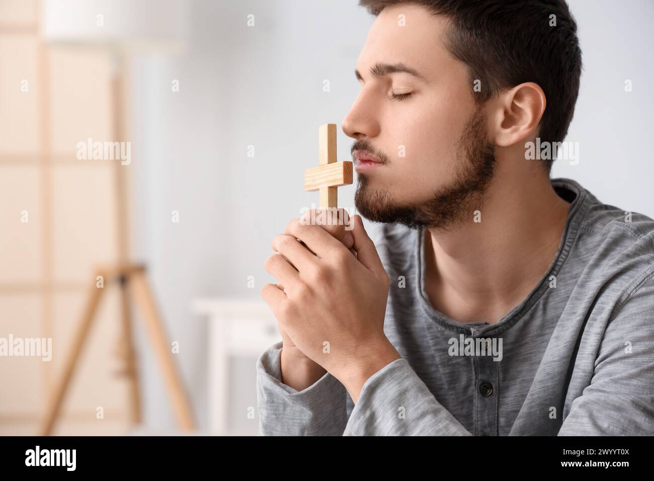 Young man with wooden cross praying in bedroom Stock Photo - Alamy