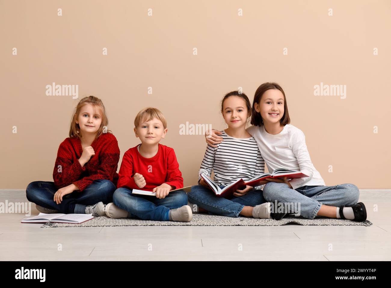 Little children reading books while sitting on floor near beige wall ...