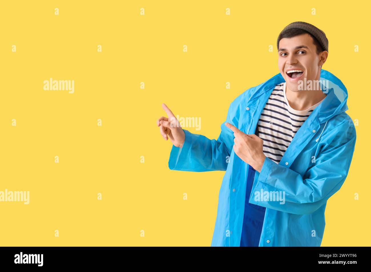 Young sailor in raincoat pointing at something on yellow background ...