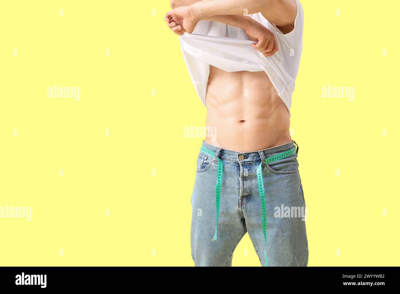 Male bodybuilder with tape measure taking off his t-shirt on yellow ...