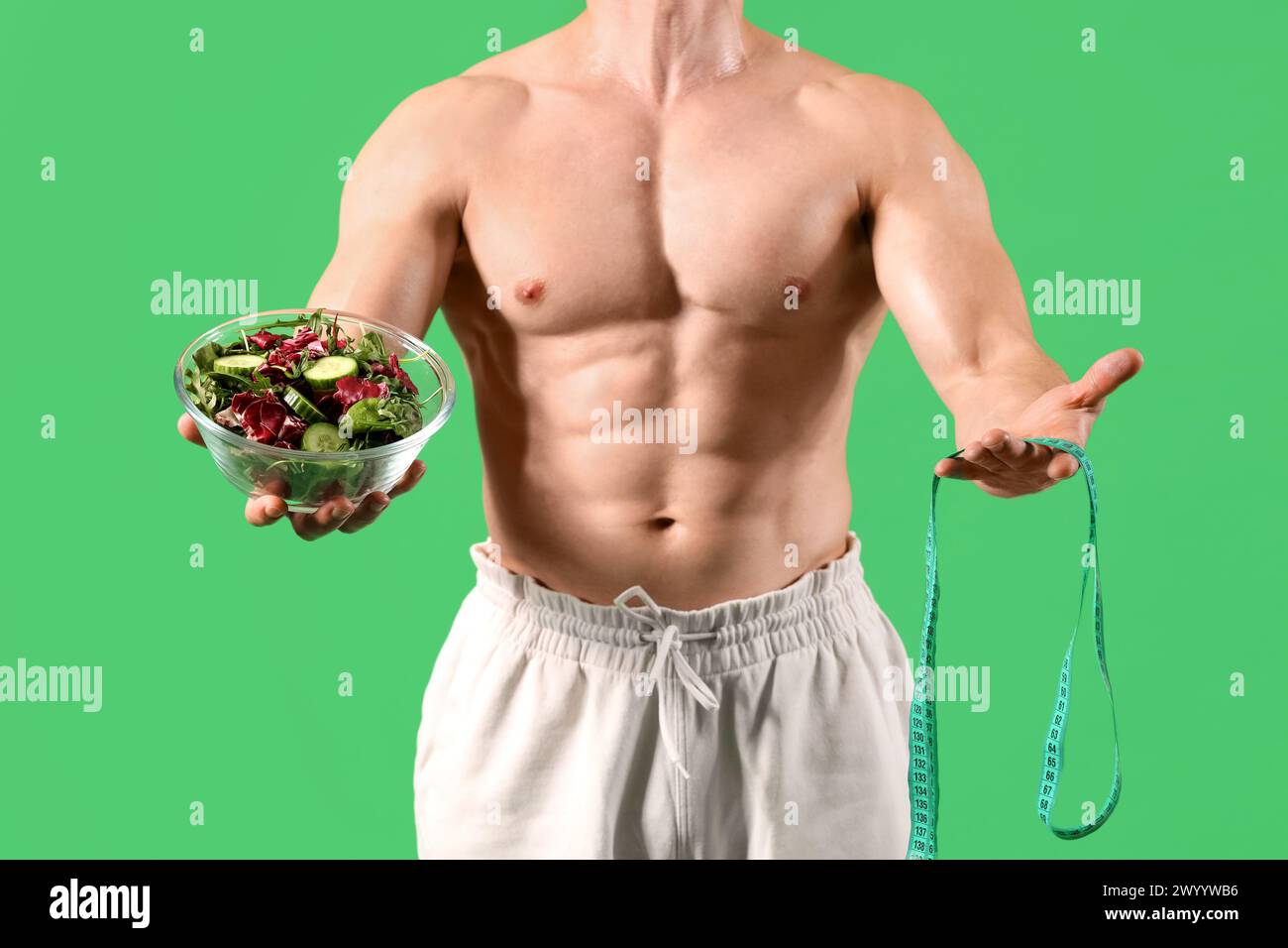 Male bodybuilder with tape measure and salad on green background ...