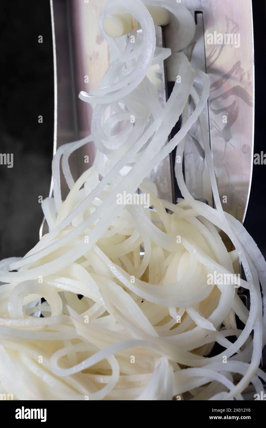 Potato on a spiralizer being cut into thin strips. On a dark stone ...
