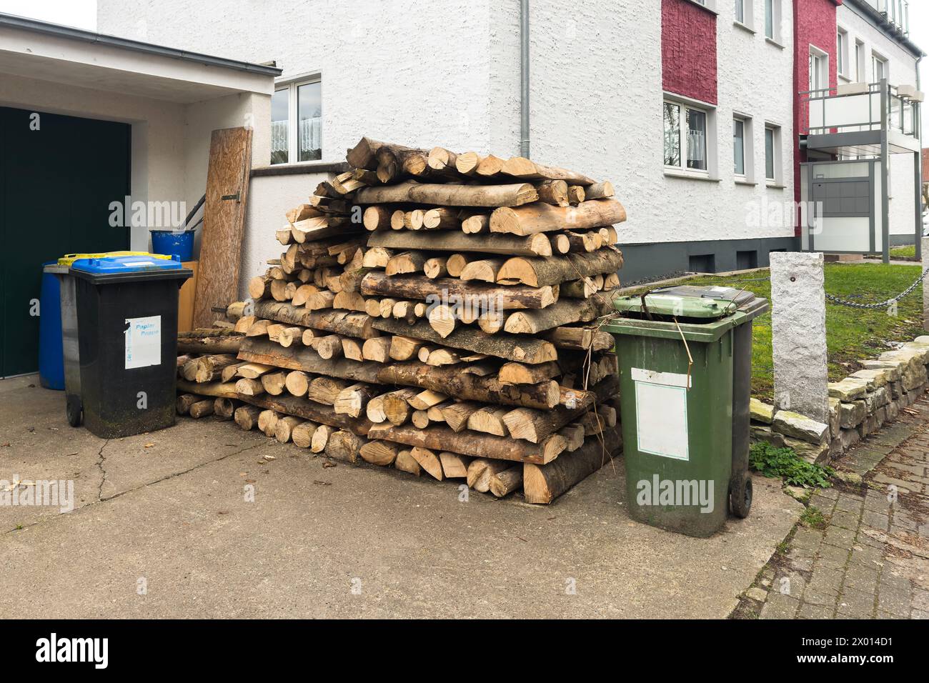 Large firewood stacked near a residential building. Plastic trash ...