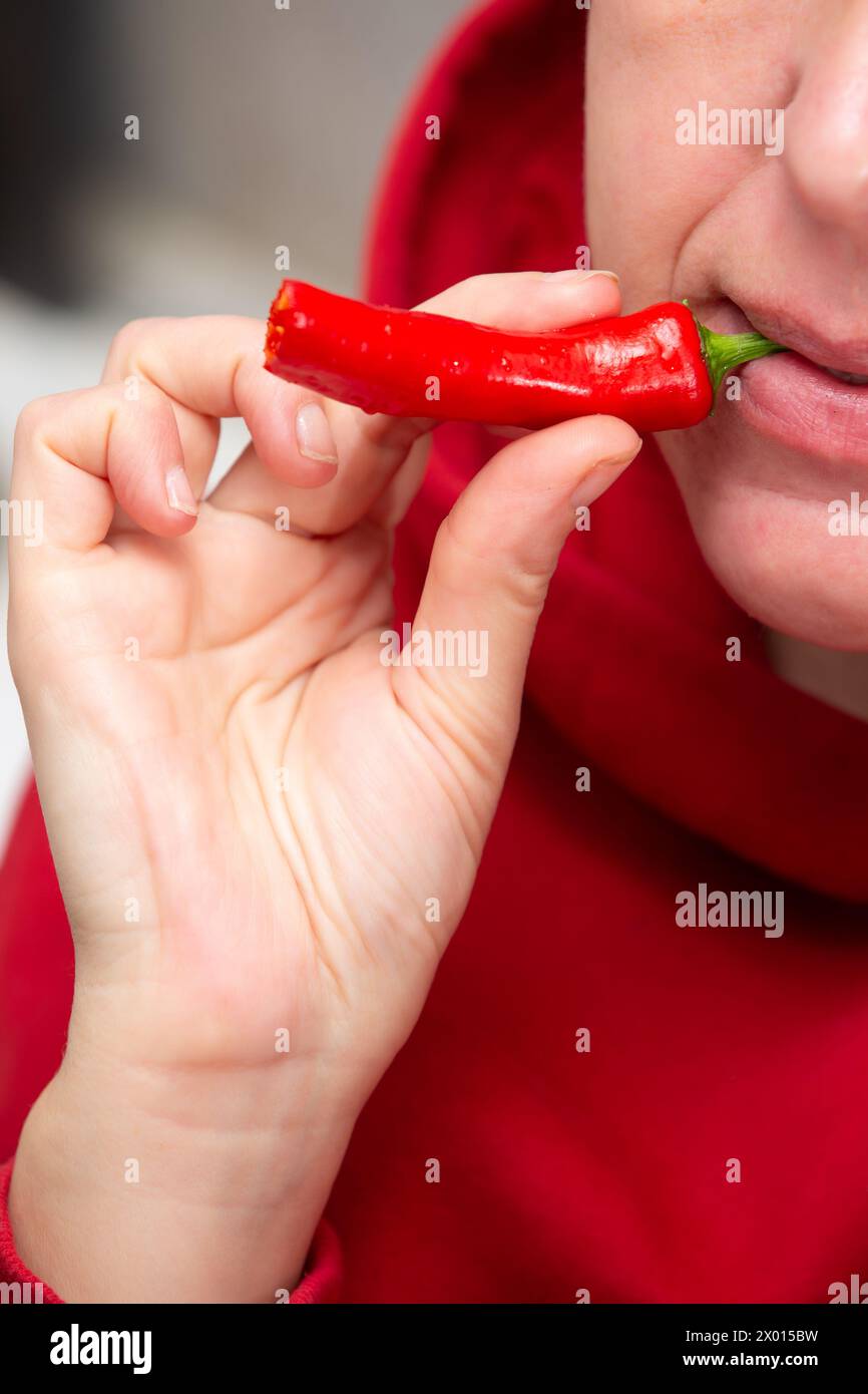 A woman, whose face is not visible, eats a red hot pepper Stock Photo ...