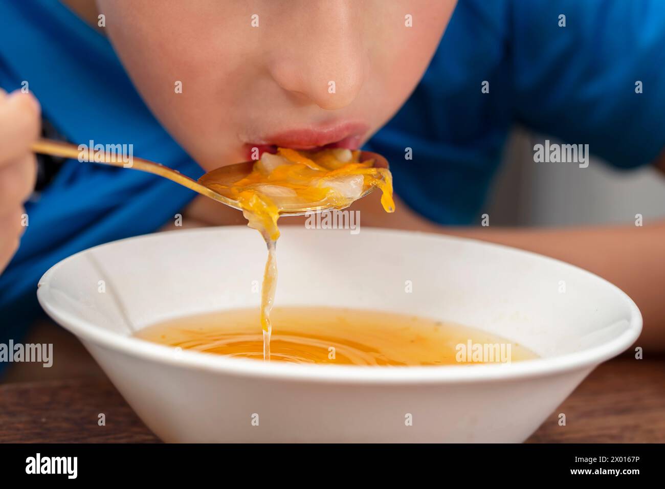 A child, whose face is not visible, eats chicken soup from a white ...
