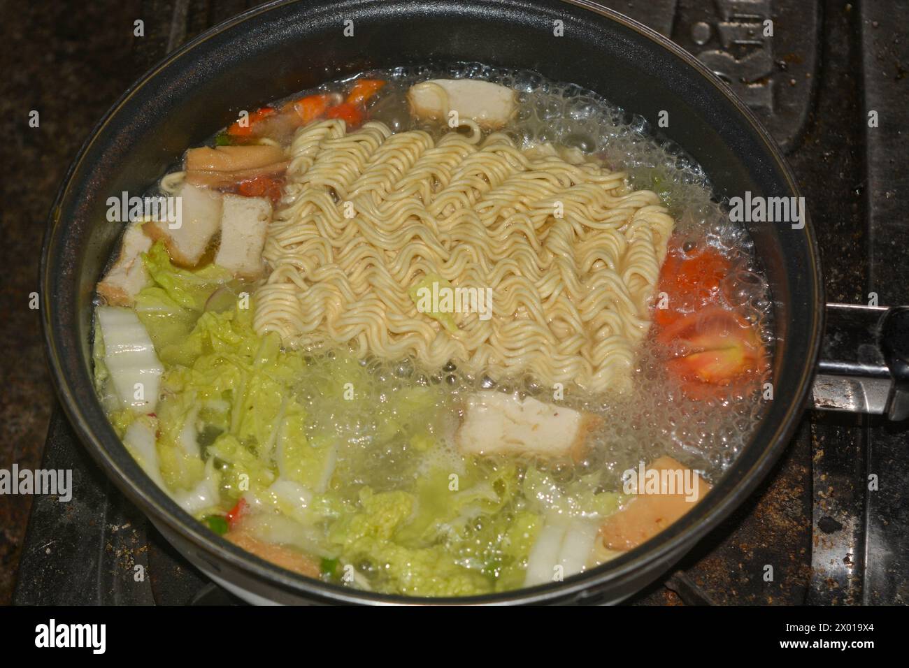 Photo of a pot of noodles being cooked with some vegetable toppings ...