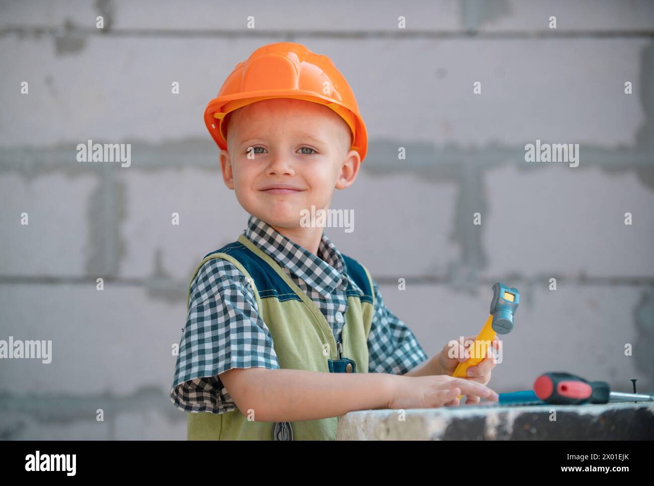 Child play with supplies, tools saw, hammer, screwdriver, helmet ...