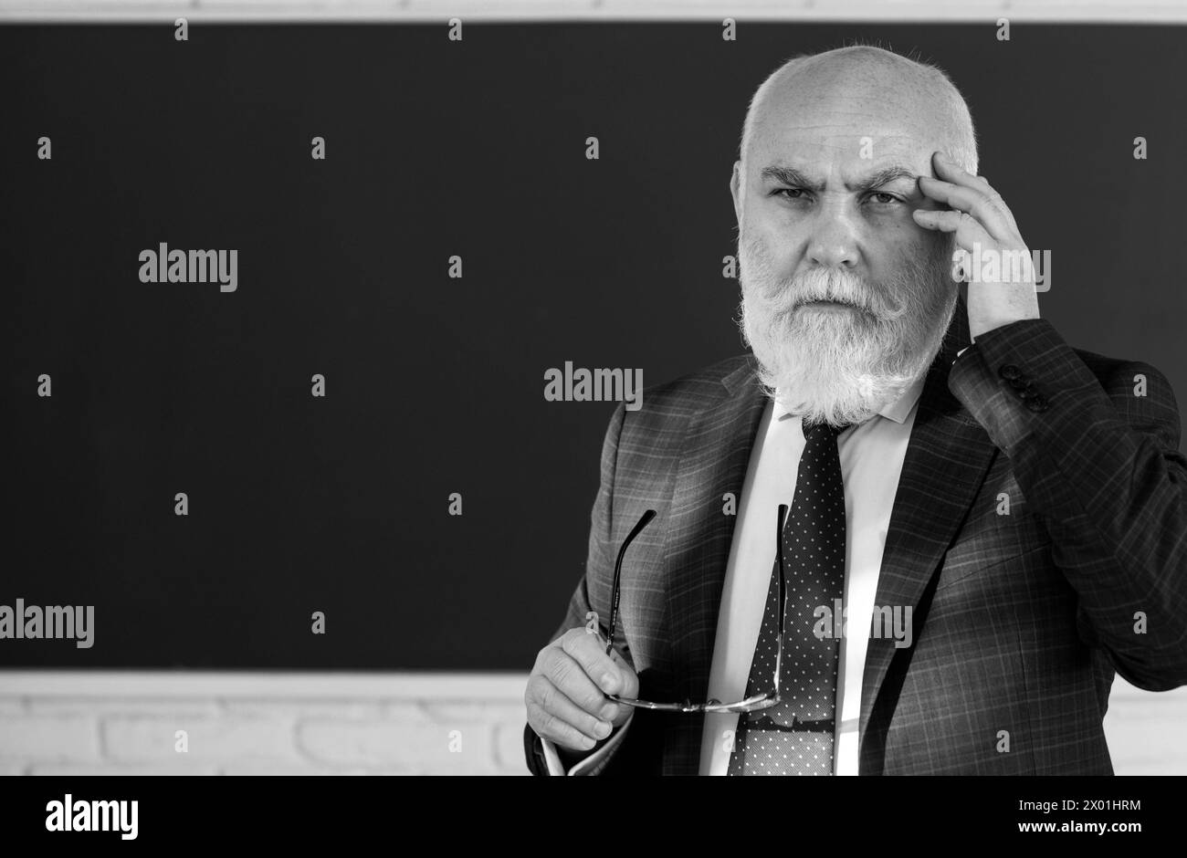 Older male thinking teacher standing in front of a chalkboard in a ...
