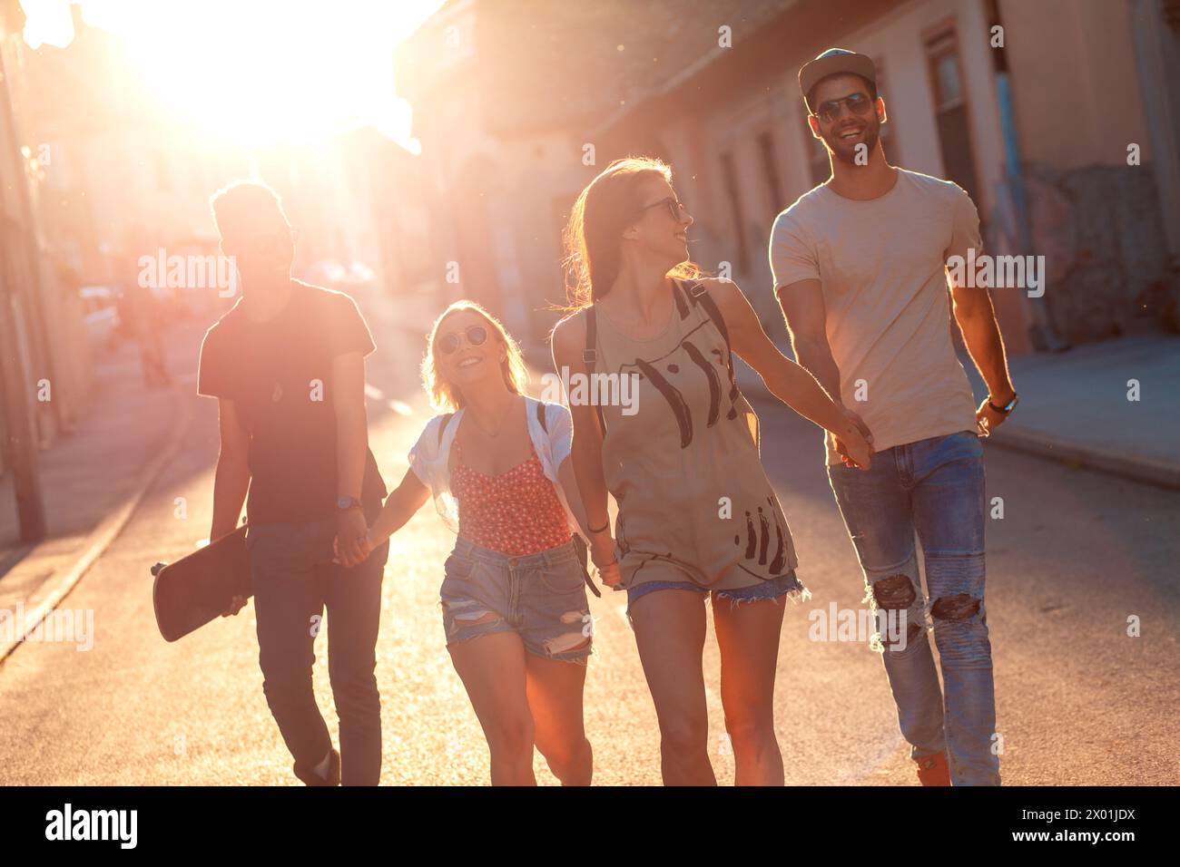 Group of friends walking and laughing at the city street at sunset ...