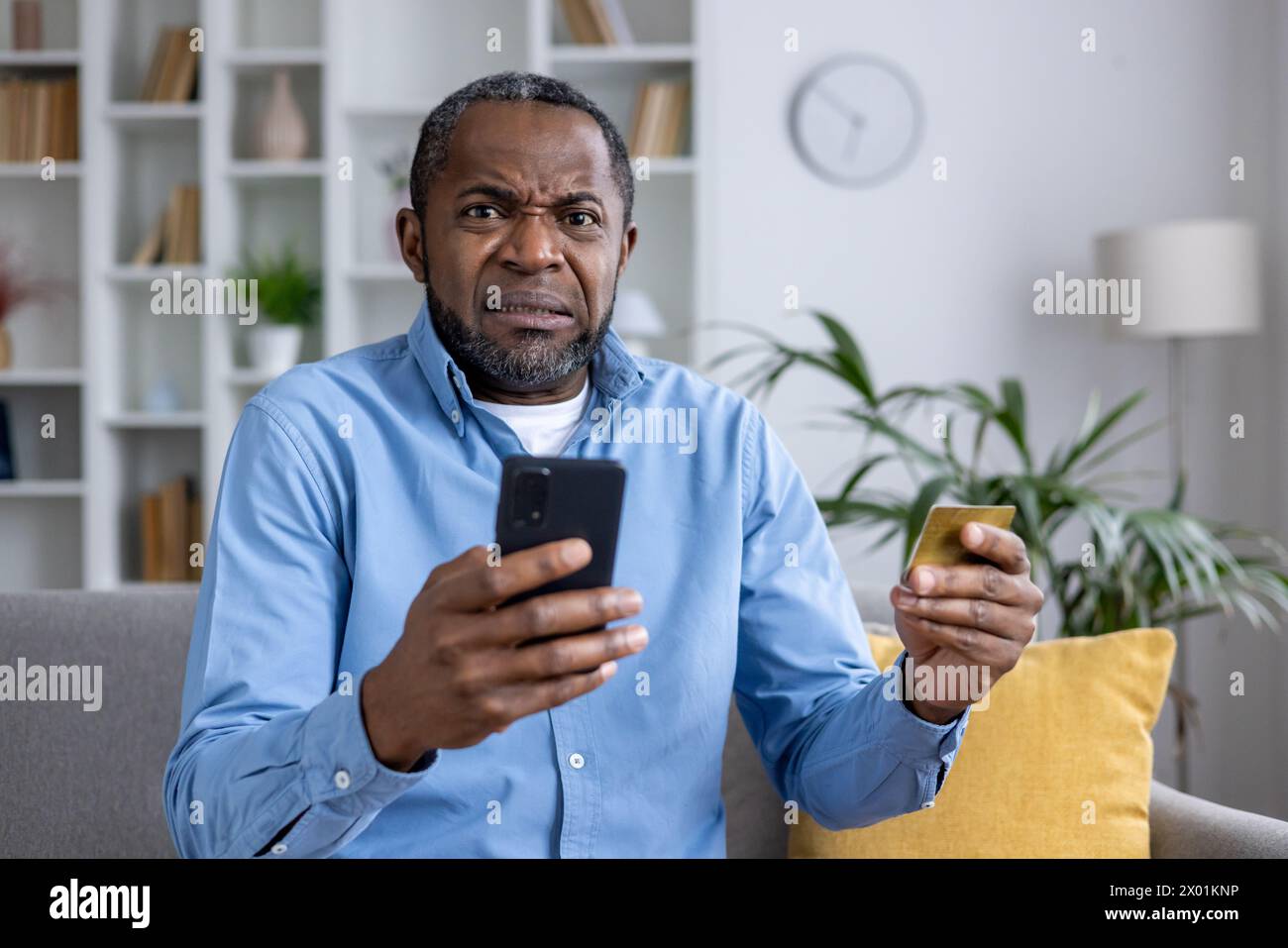 Focused man sitting at home with credit card and smartphone, possibly a ...