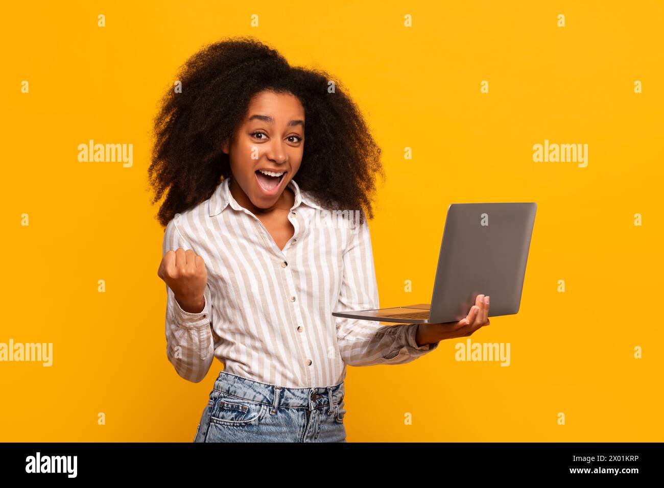 Excited woman holding laptop with fist pump Stock Photo - Alamy