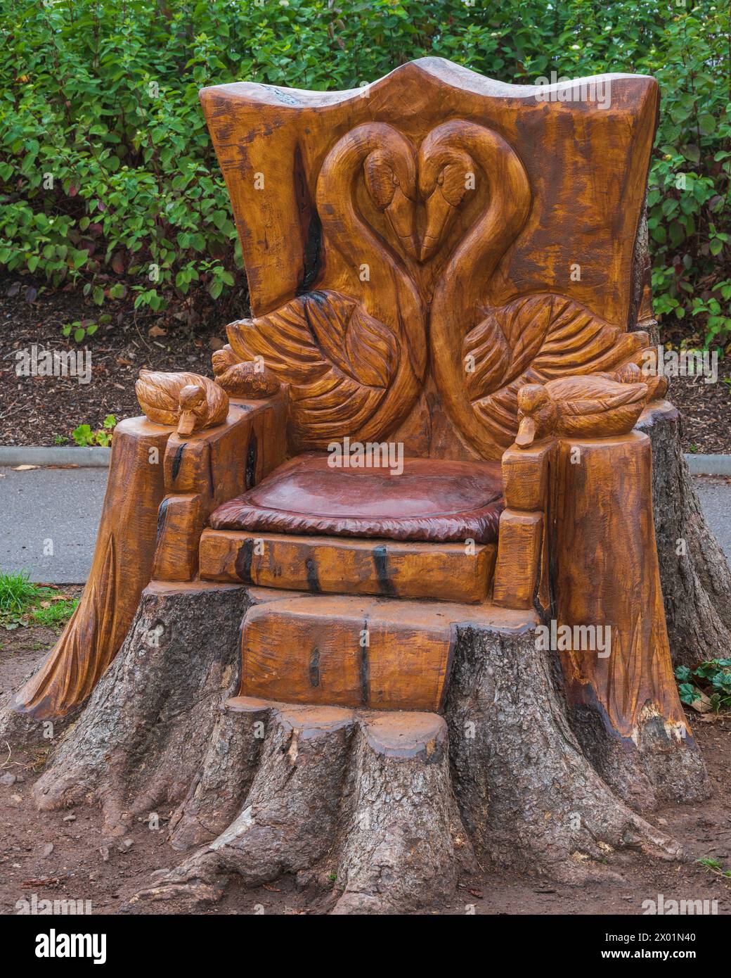 An old tree stump, cleverly carved into a chair with two swans on the ...