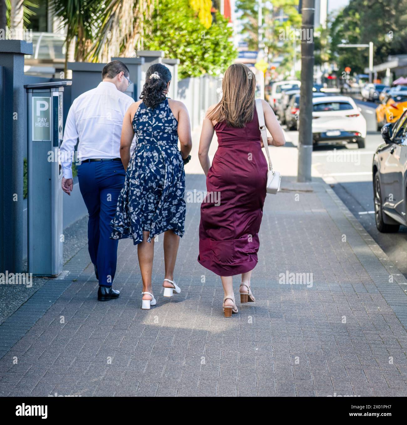 Three young people walking on the pedestrian footpath along a busy ...
