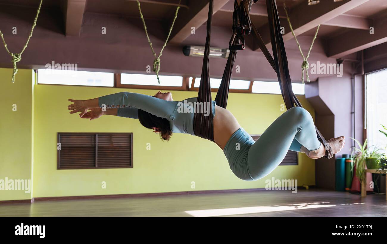 A woman of European appearance is engaged in aerial yoga, performs the ...