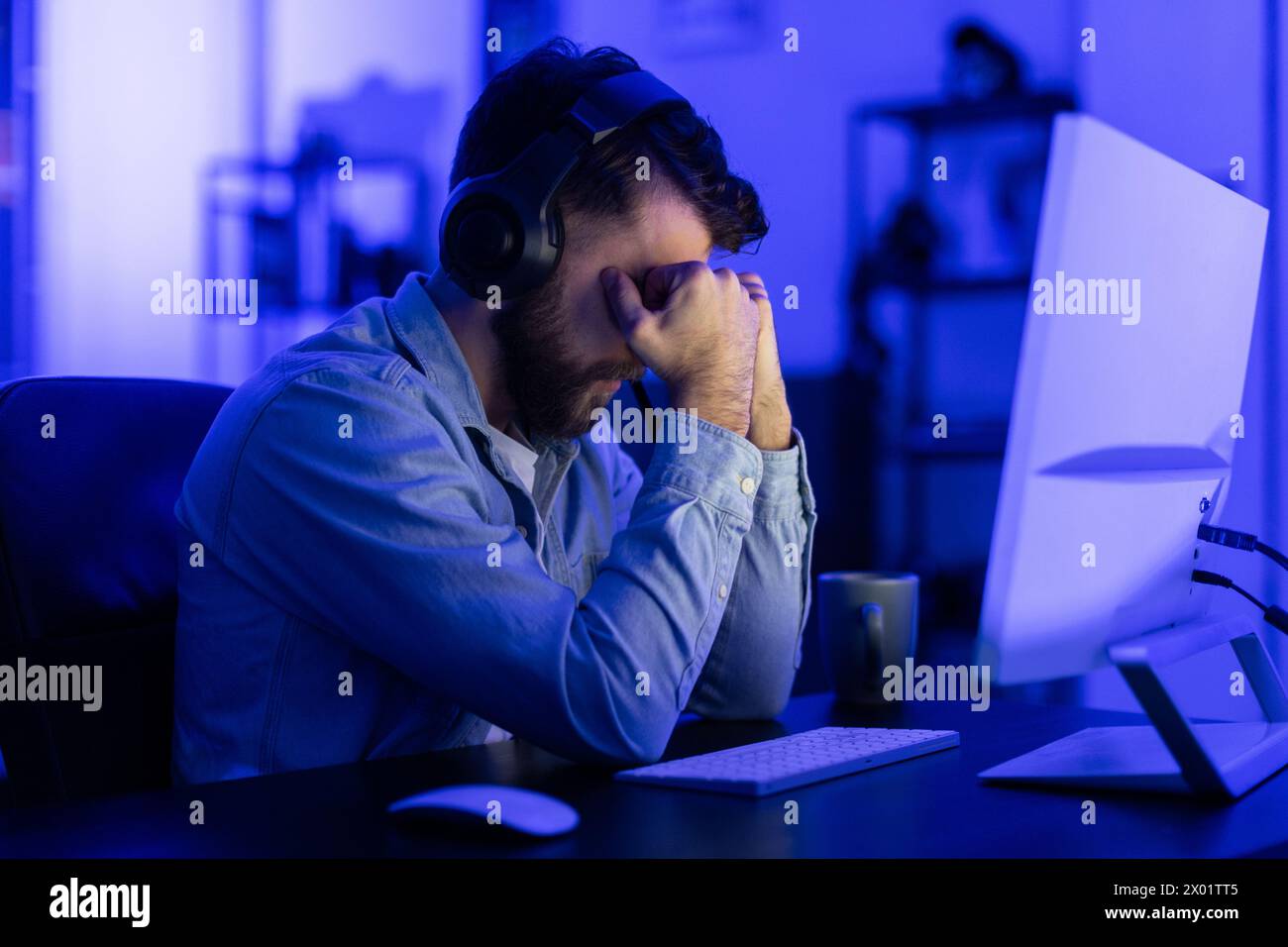 Stressed man at computer holding head in neon light Stock Photo - Alamy