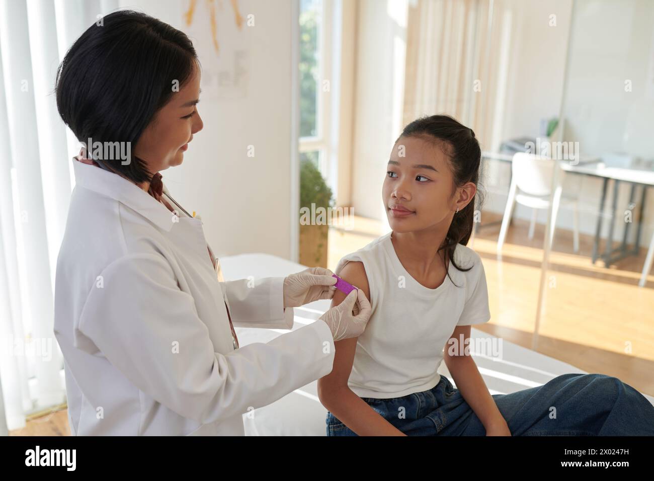 Smiling doctor sticking bandage on injection site on arm of teenage ...