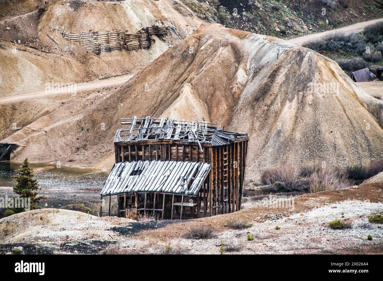 Decaying wooden mining building against vividly colored earthy mounds ...